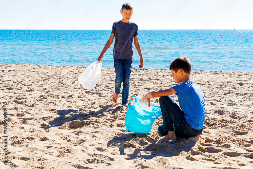 Volunteers cleaning beach from plastic. Boys walking on the beach and ...