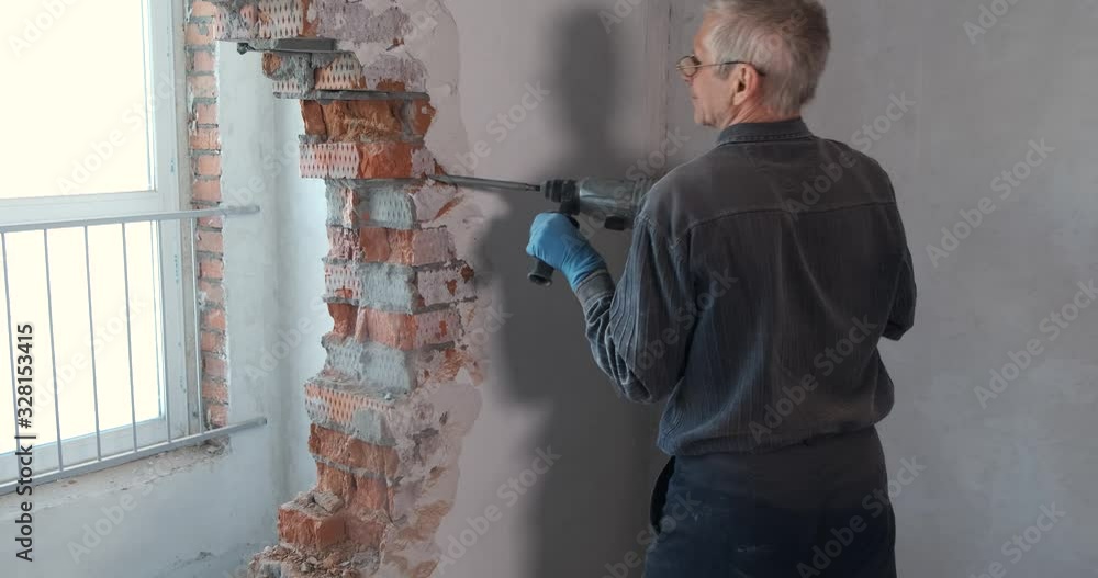 Builder works at construction site, man destroys thick brick wall ...