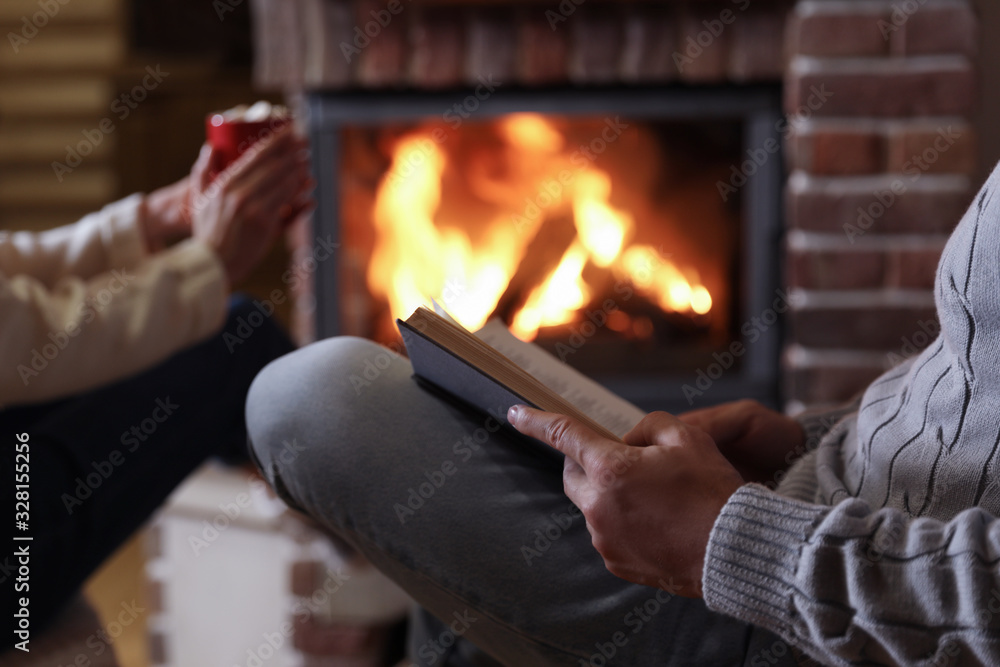 Man reading book and his girlfriend near burning fireplace at home ...