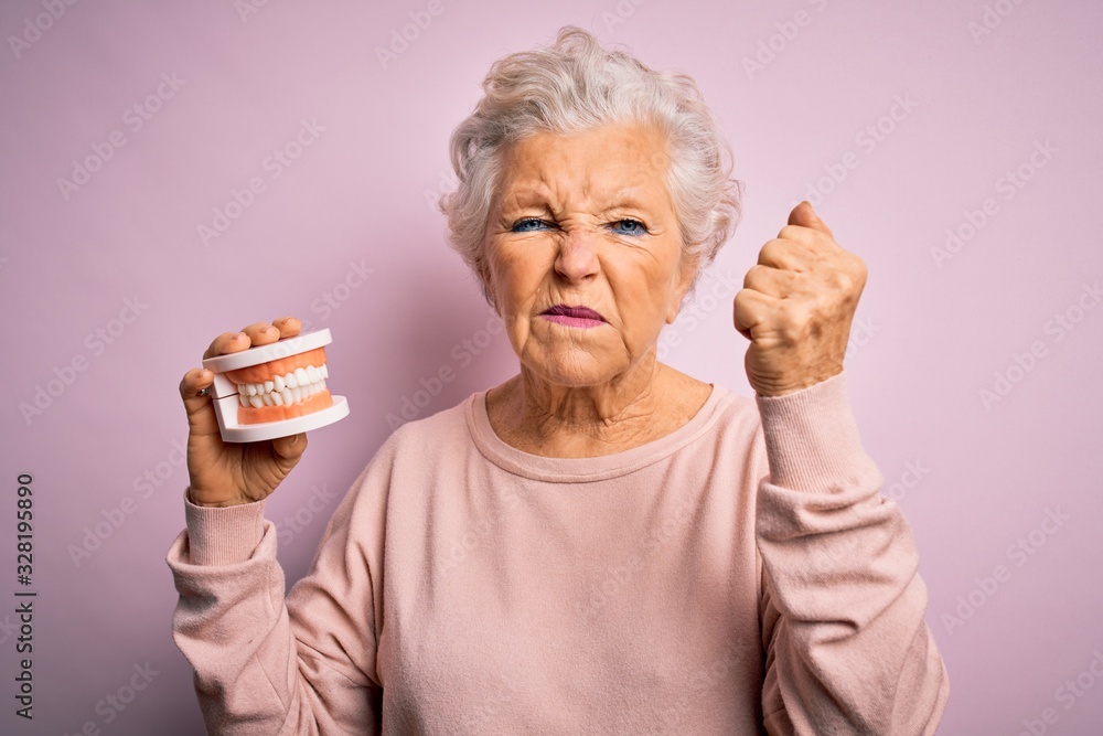 Senior beautiful grey-haired woman holding plastic denture teeth over ...