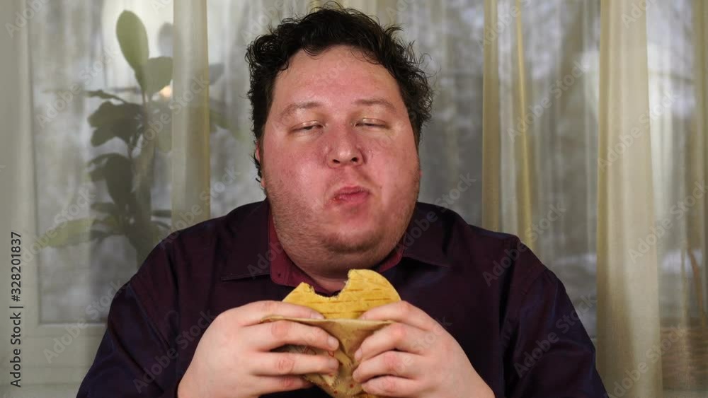 Young man bites sandwich. Fat guy eats fast food. Very hungry guy ...