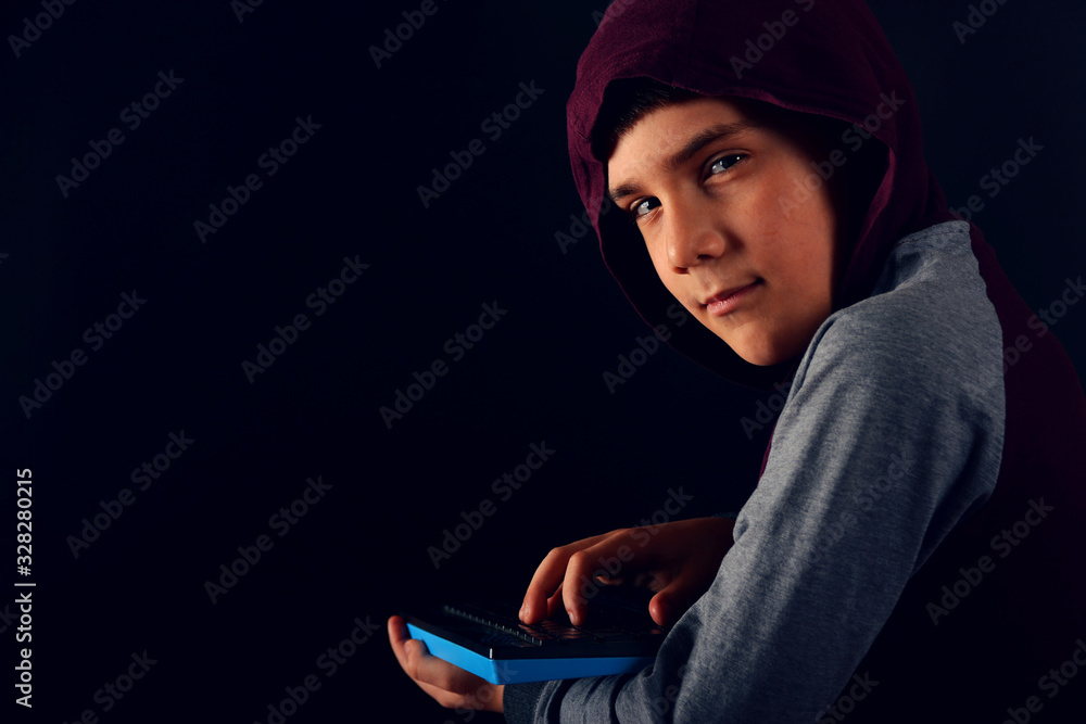 Frightened and angry boy in the hood, a young hacker, looks around ...