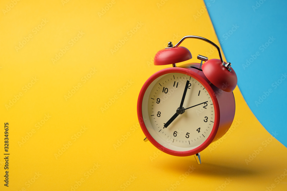 Red retro alarm clock floating in the air with yellow and blue ...