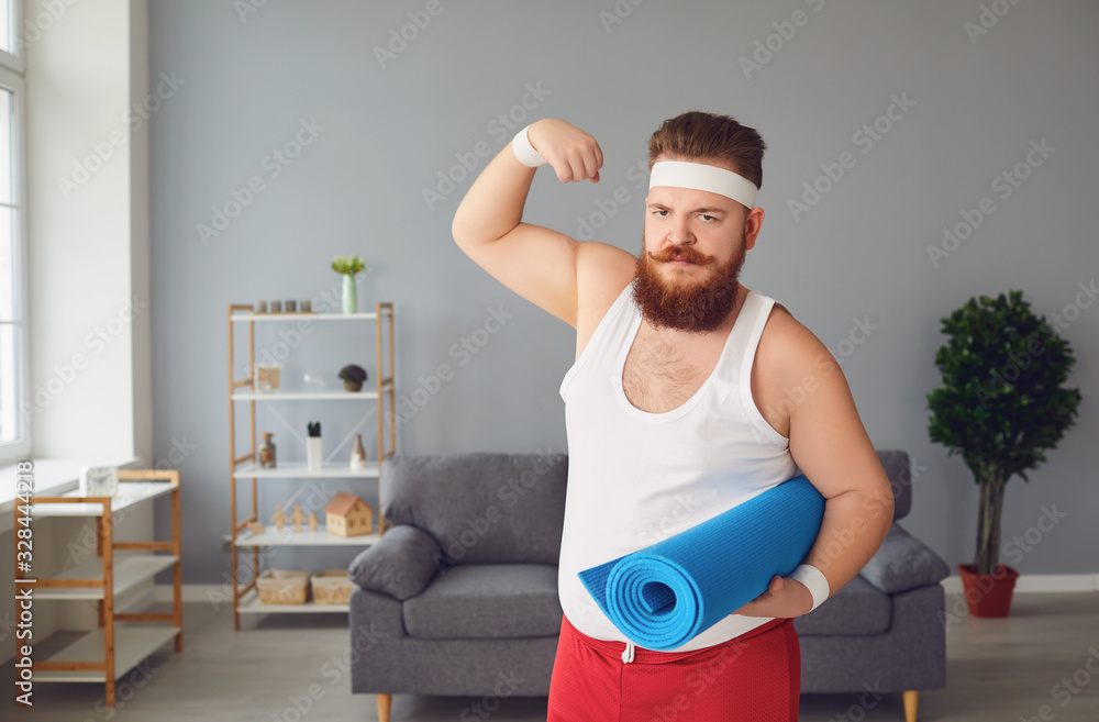 Funny fat man in sportswear shows muscles standing in the room at home ...