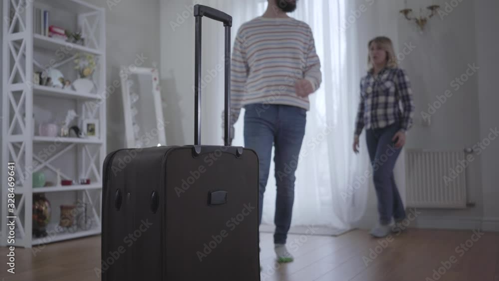 Young angry Caucasian man pushing away wife, taking travel bag and ...