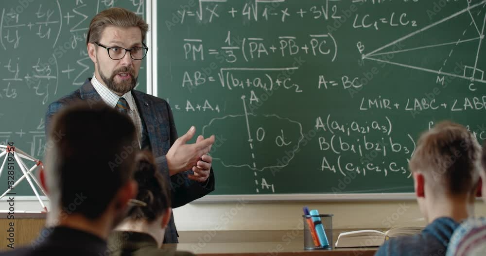 Middle aged math teacher in suit and eyewear giving lesson to students ...