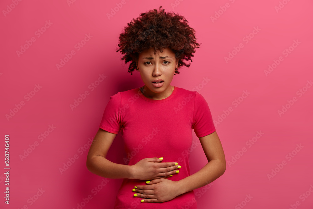 Unhappy African American female feels unwell, has stomach ache because ...