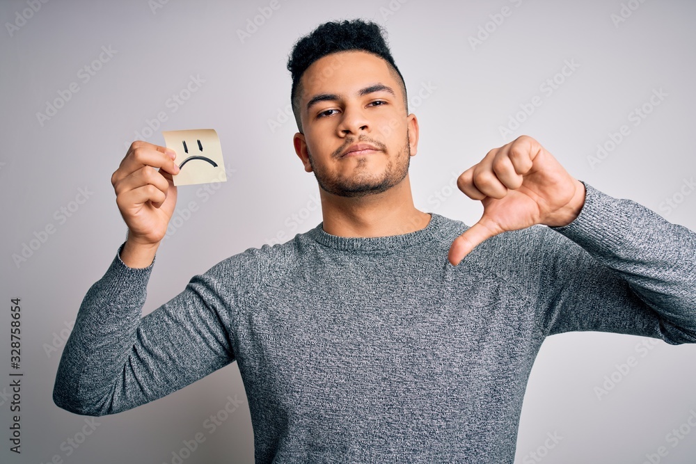 Handsome man holding reminder paper with sad emotion face emoji over ...
