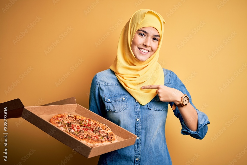 Young girl wearing muslim hijab holding box with Italian pizza over ...