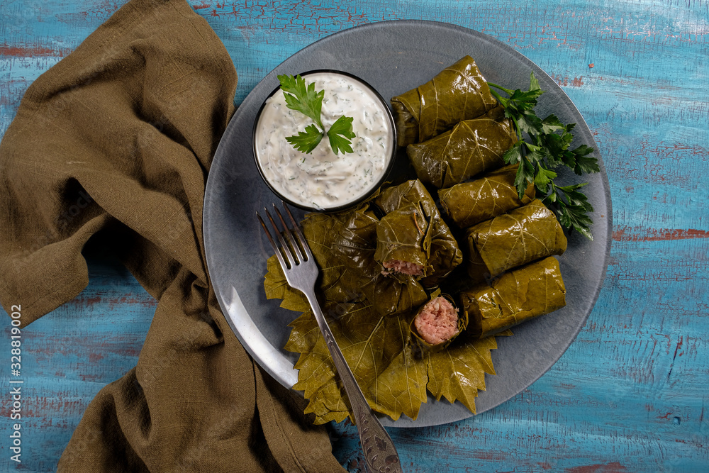 Traditional Georgian dolma in grape leaves on a wooden table with sour ...