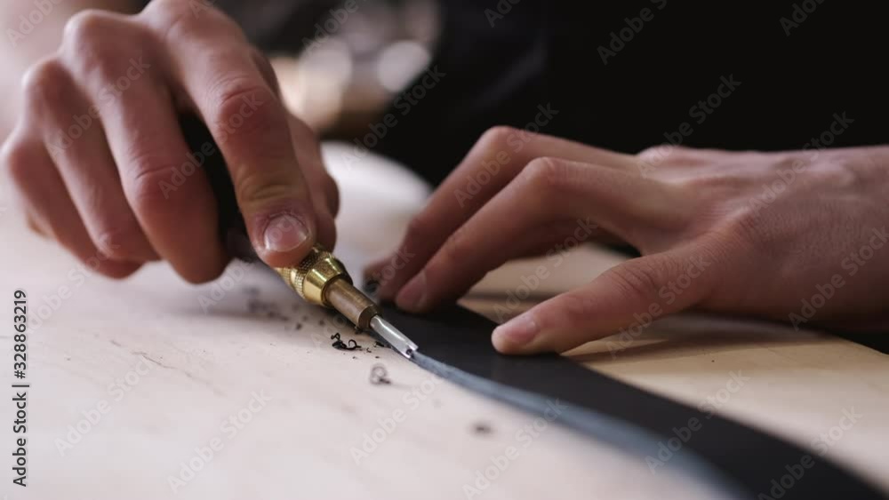 A leather craftsman is cutting the edges of a belt. The master is using ...
