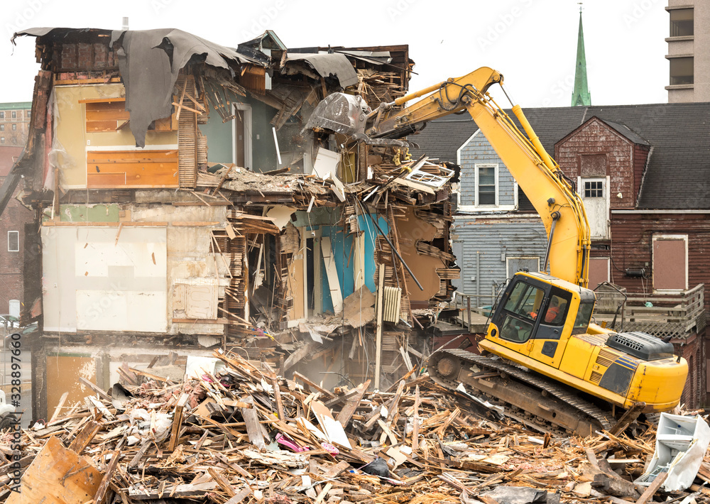 Demolishing a building with a large backhoe. Overcast day. Air is dusty ...