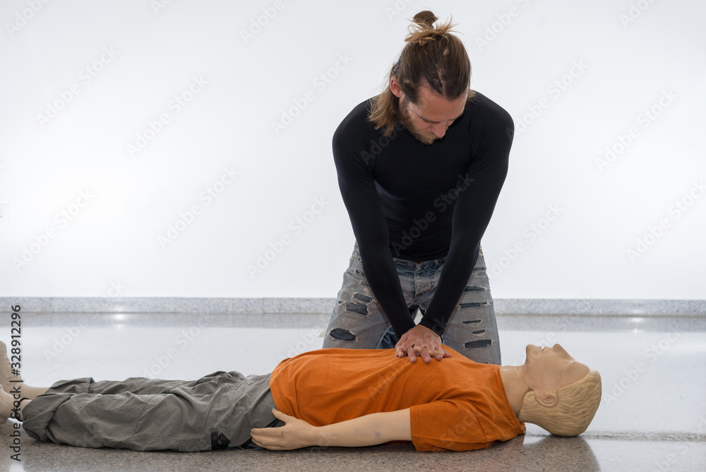 Man teaching cardiopulmonary resuscitation with a dummy on a white ...