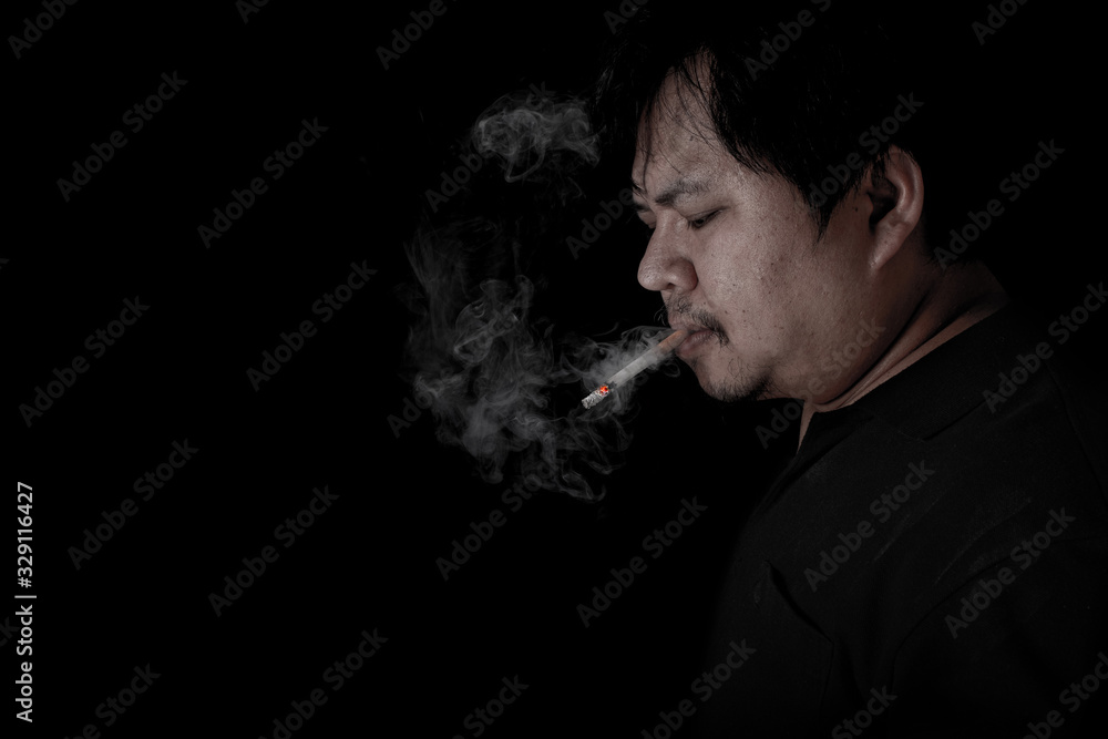 The fat man was wearing a black shirt smoking at the black background ...