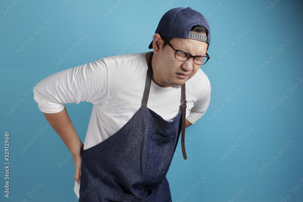 Young Asian male chef or waiter wearing blue apron suffer from lower ...