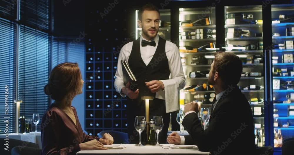 Caucasian young male waiter coming to table of couple clients and ...
