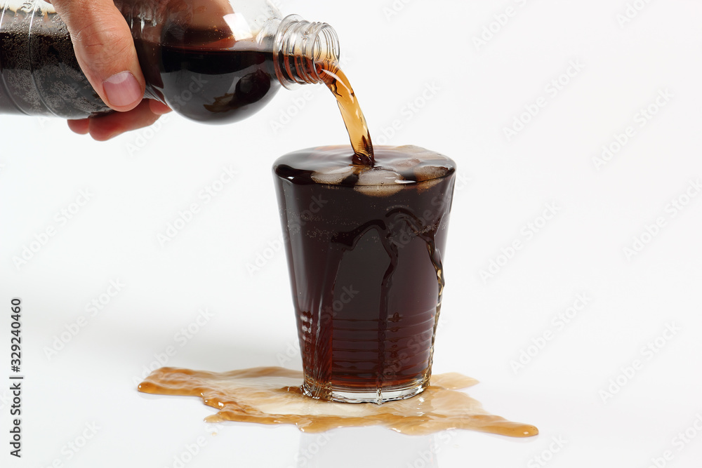 Human hand pouring cola from plastic bottle into overflowing glass with ...