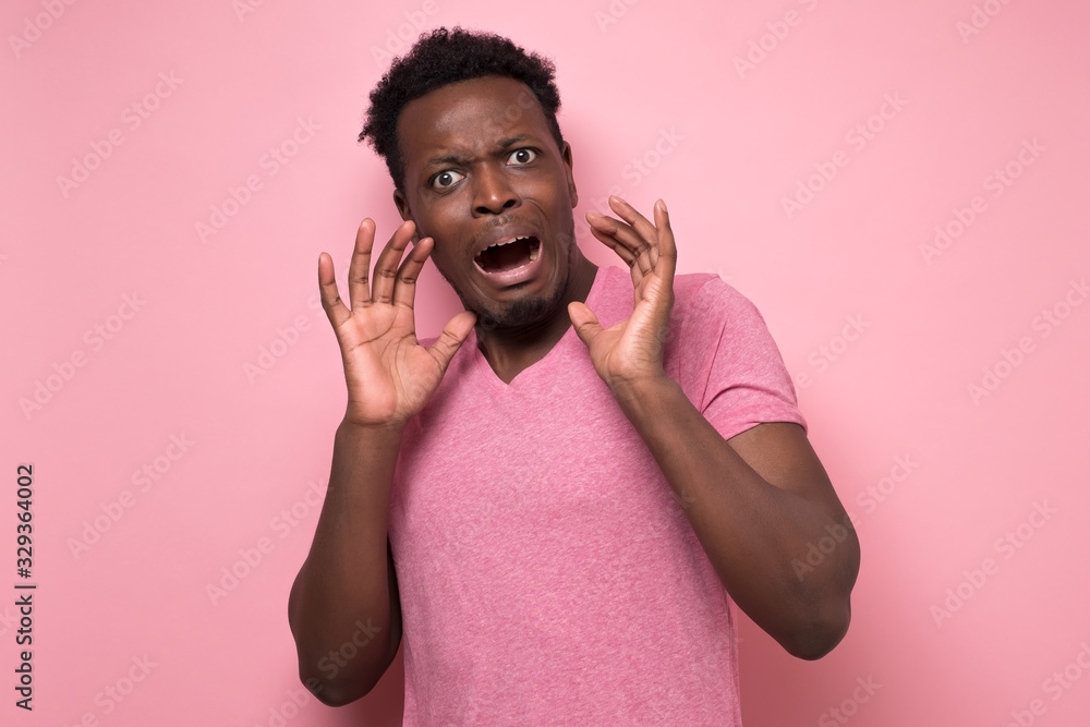 Funny african american scared man in pink shirt with worried expression ...