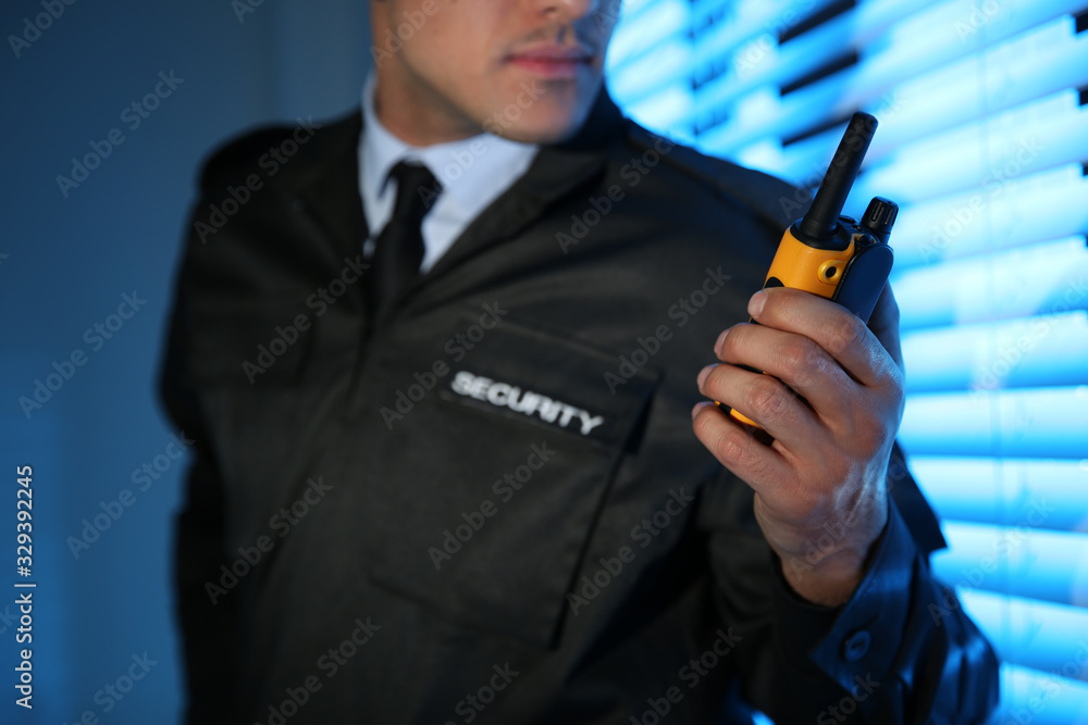 Professional security guard with portable radio set near window in dark ...