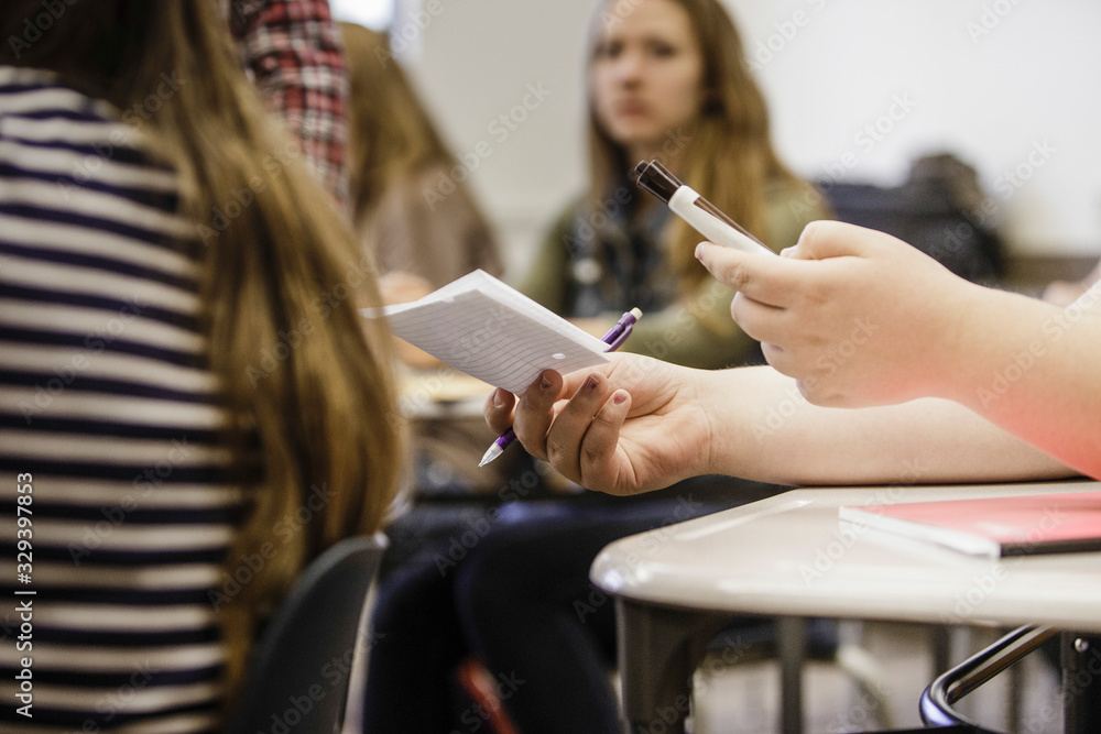 Teenage school kids passing notes in the classroom during class. Red ...