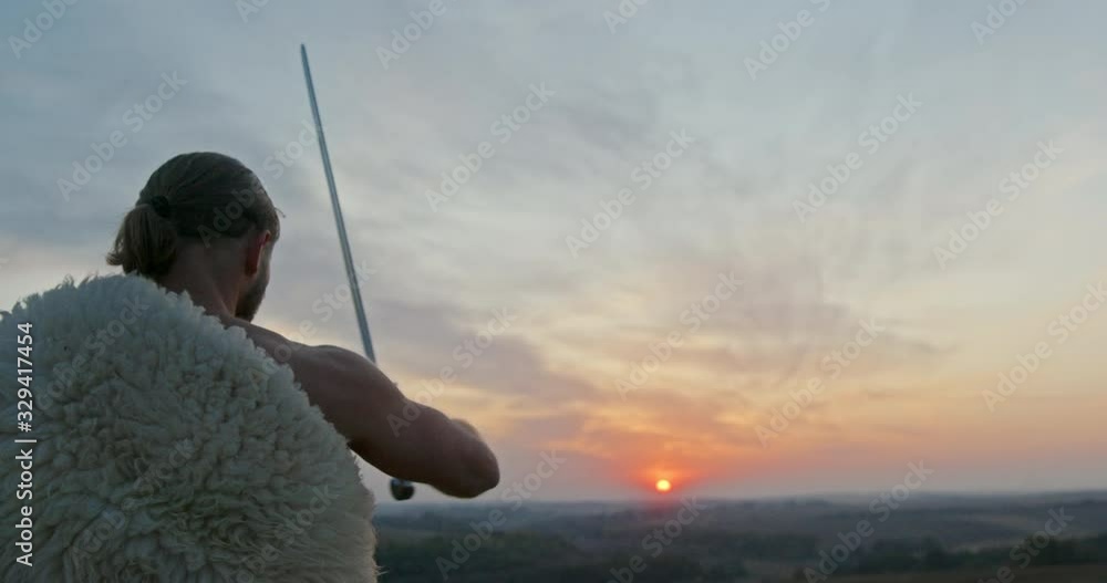 Man wearing a sheepskin holding a sword in his hand as he faces towards ...
