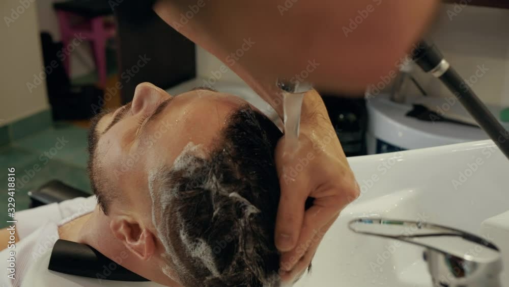 Hairstylist hand washing of shampoo foam from male hair with water in ...