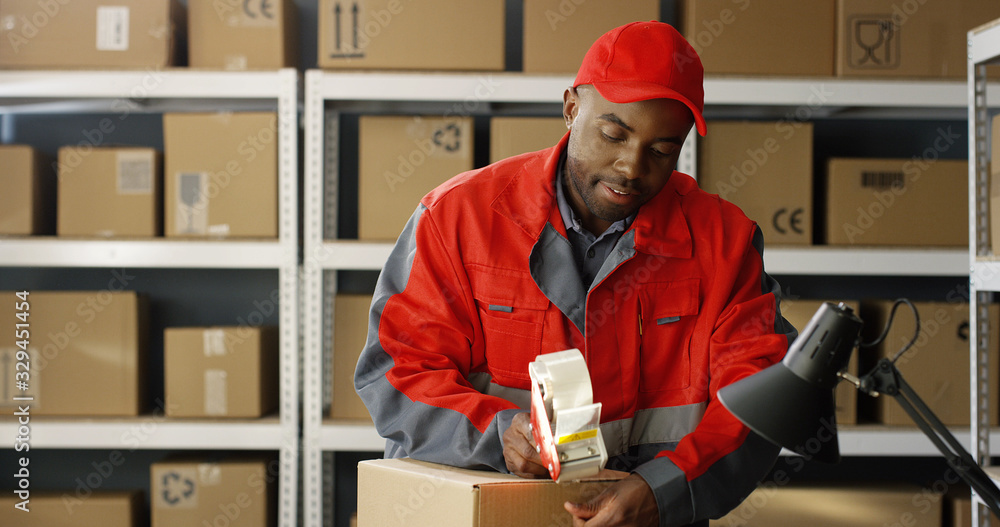 African American postal male worker in uniform packing carton box at ...