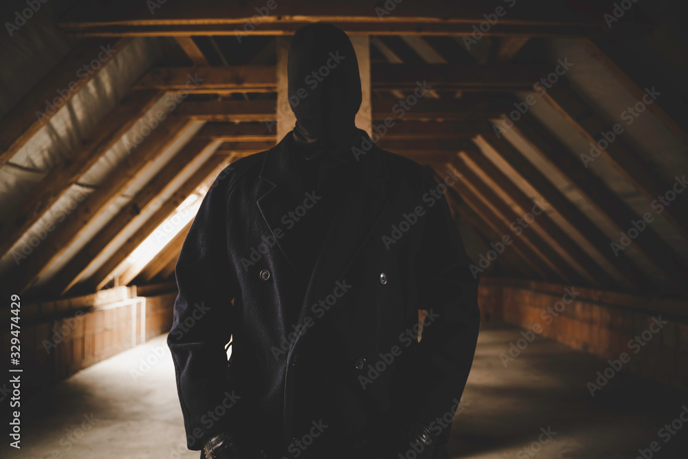 A scary guy in black mask and long dark coat standing in an abandoned ...