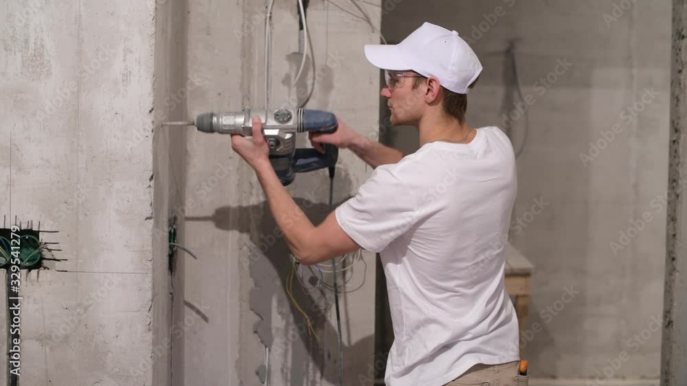 A young worker in a white uniform drills a wall with a punch in a ...