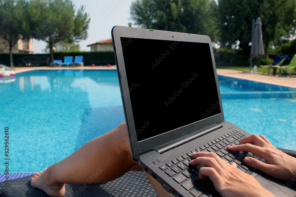 Screen mockup of laptop used by young woman laying near swimming pool ...