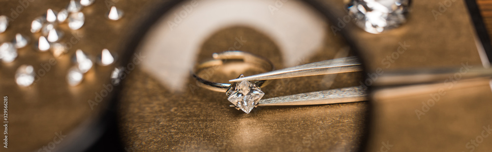Selective focus of magnifying glass, jewelry ring with gemstone in ...