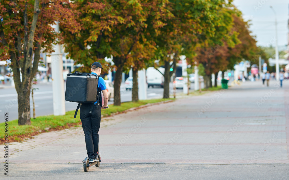 Delivery boy on electric scooter with backpack riding fast on pavement ...