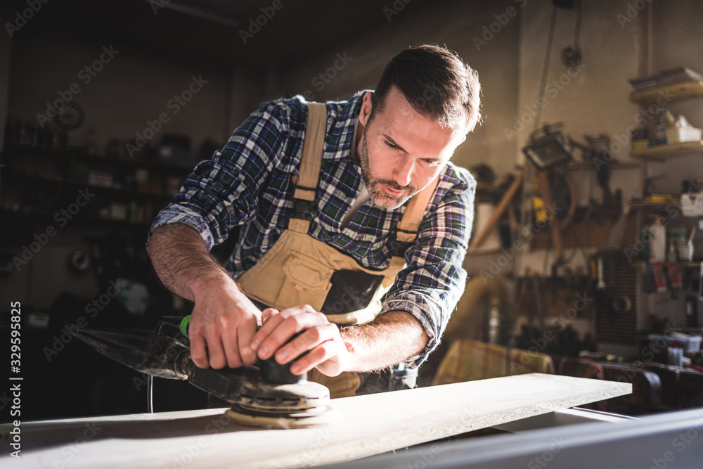 Carpenter at workshop polishes wooden board with a electric orbital ...