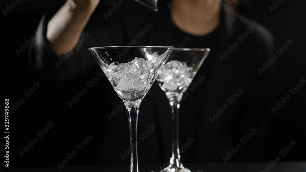 Ice cubes falling into empty glass in slow motion. Close up. Female bartender making cocktails ...