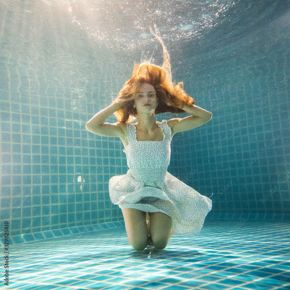 Beautiful woman with long red hair posing underwater in white dress ...