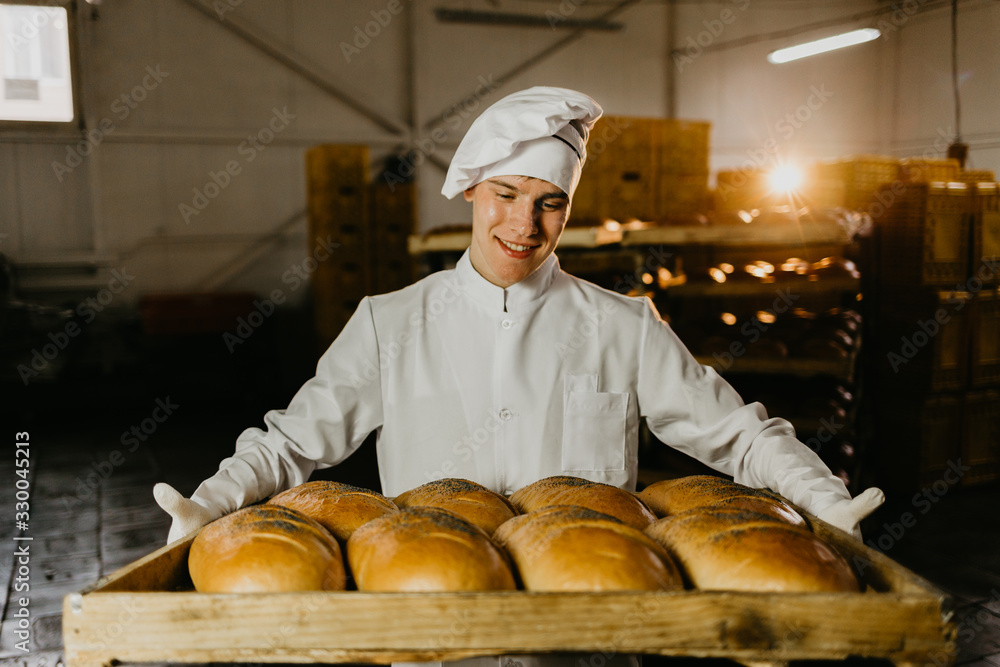 A baker holds a tray with fresh hot bread in his hands against the ...