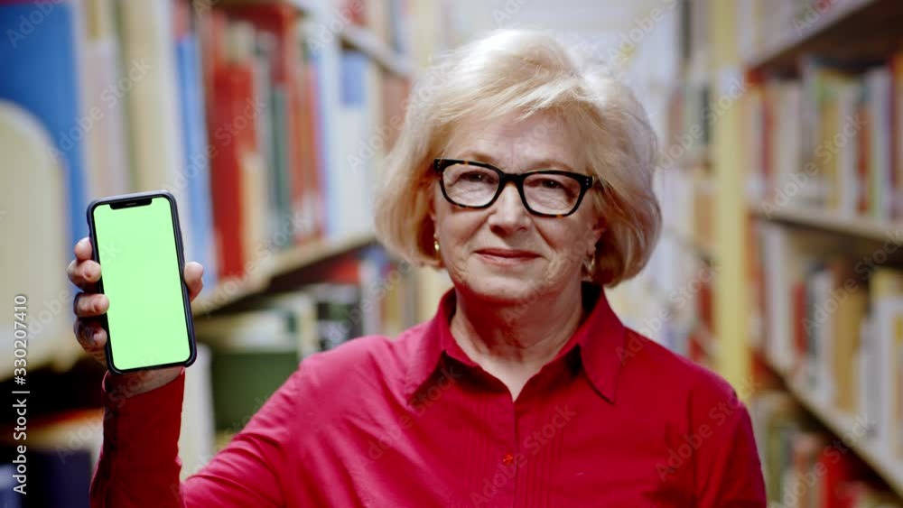 Portrait of beautiful old lady librarian holding a vertical smartphone ...