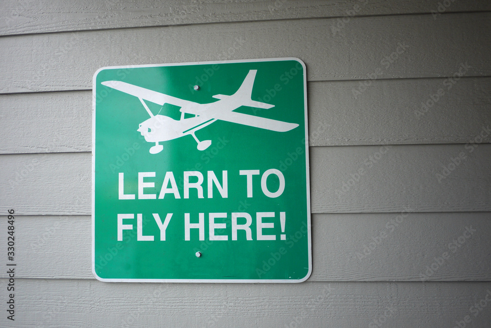 Airport Sign "Learn To Fly Here" with exterior wall background. Stock ...