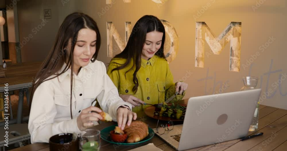 Two attractive women in stylish outfit eating tasty food while sitting ...