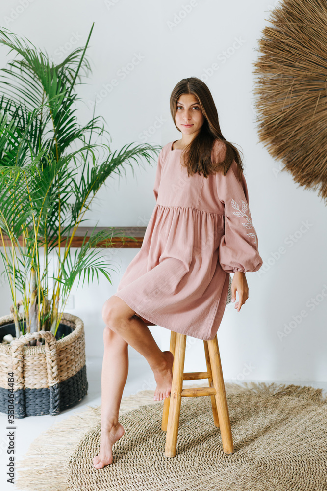 Stylish emotionless young woman in a pink dress posing in a tropical ...