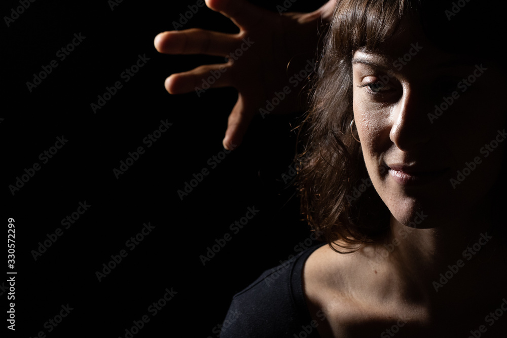 Low key photo of sad worrying brunette woman against black background ...
