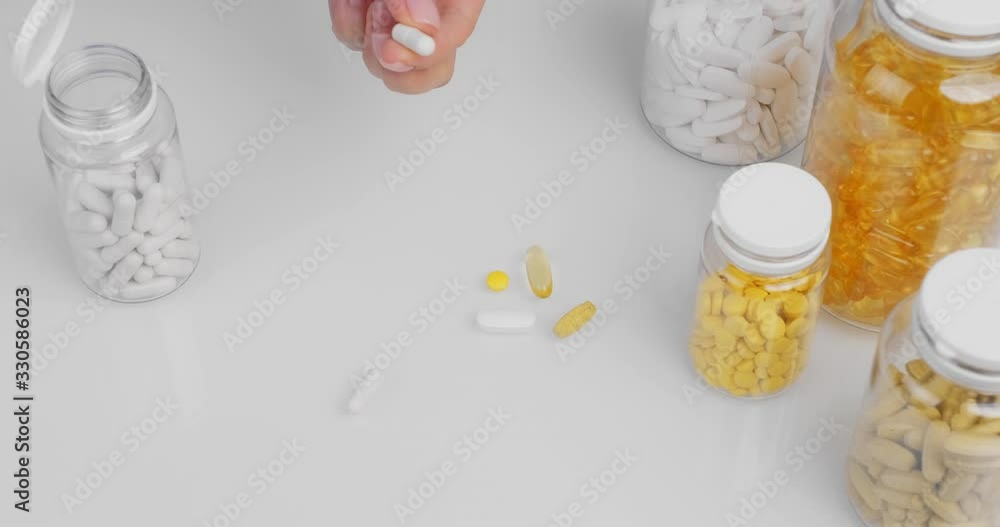 Close-up woman's hand pouring white capsules bottle surface, takes one ...