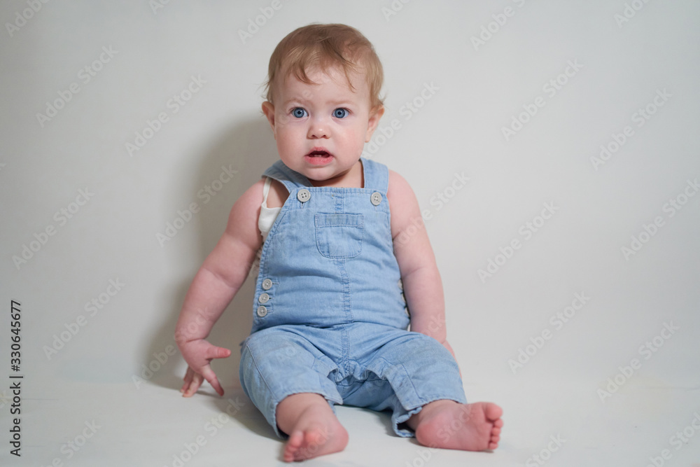 emotional portrait of a one-year-old baby in denim overalls on a ...