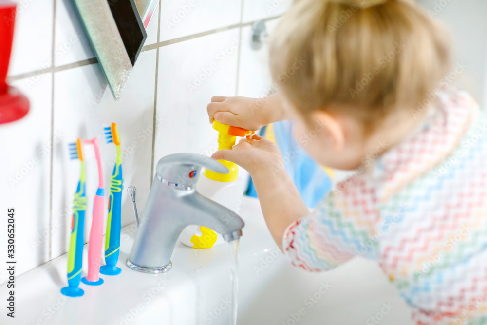 Cute little toddler girl washing hands with soap and water in bathroom ...