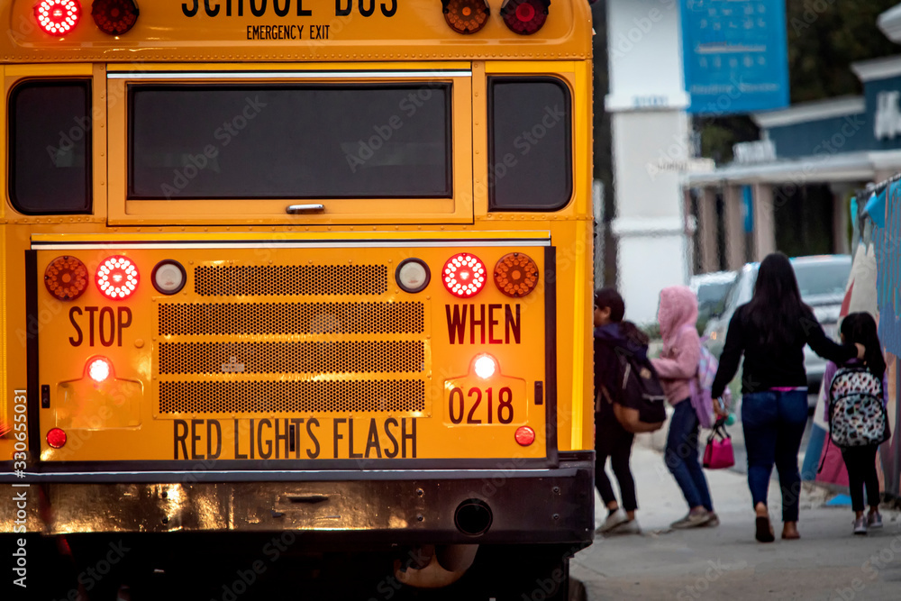 School bus with flashing lights and children boarding diffused in the ...