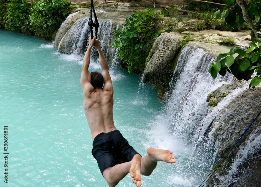 Man jumping from cliff into natural pool before waterfall , in air ...