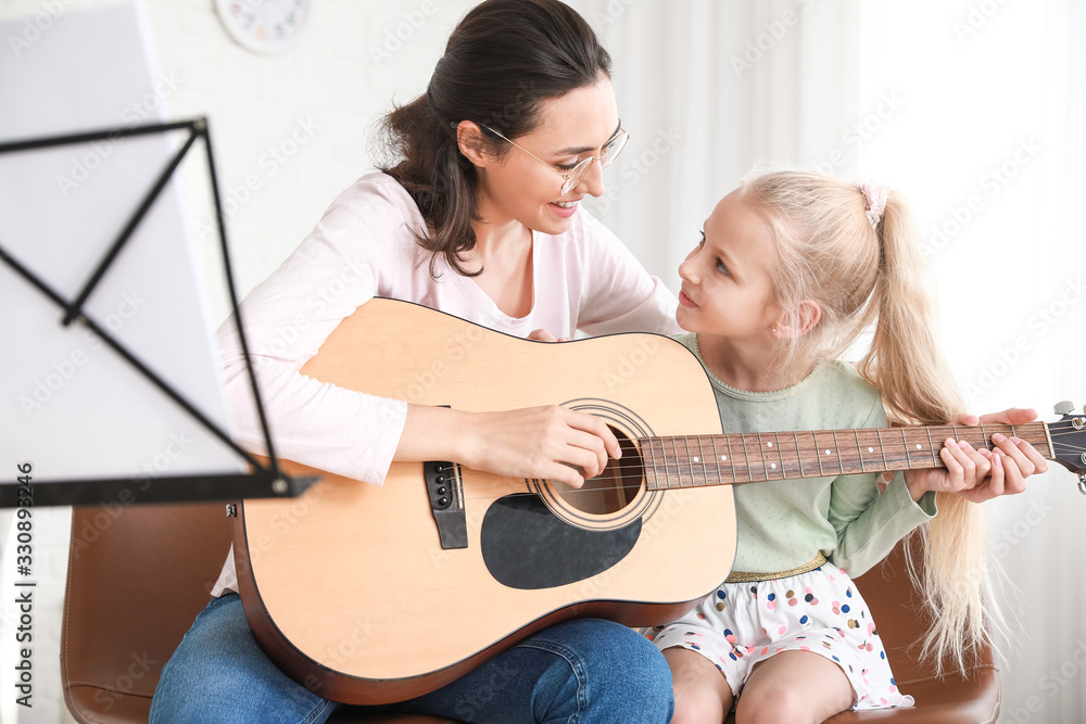 Private music teacher giving guitar lessons to little girl at home ...