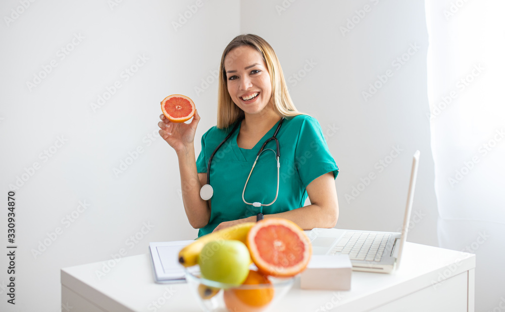 Female nutritionist with fruits working at her desk. Smiling ...