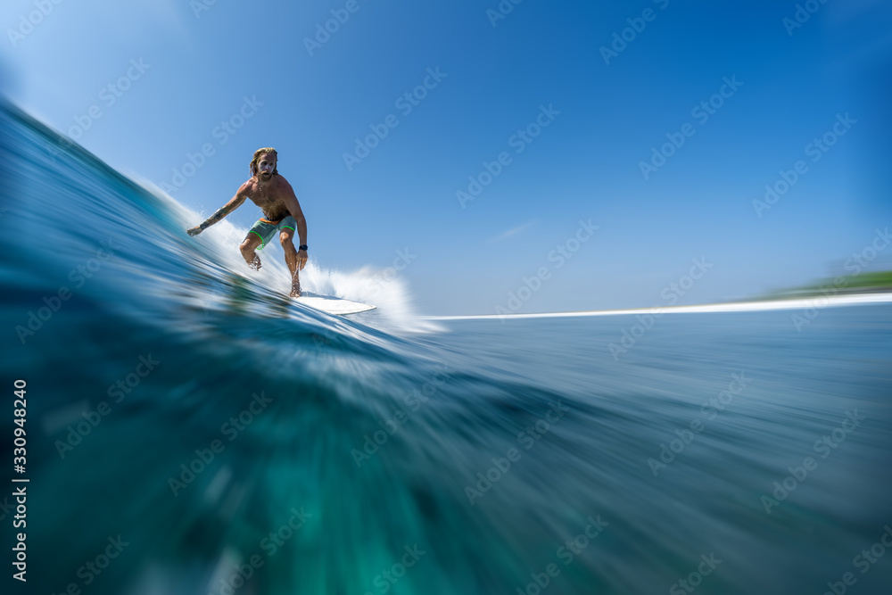Young man surfer with long hair surfs the fast and perfect ocean wave ...