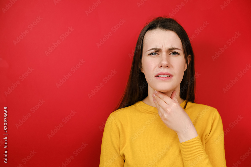 Tired young female model has sore throat, being sick and unwell, frowns ...